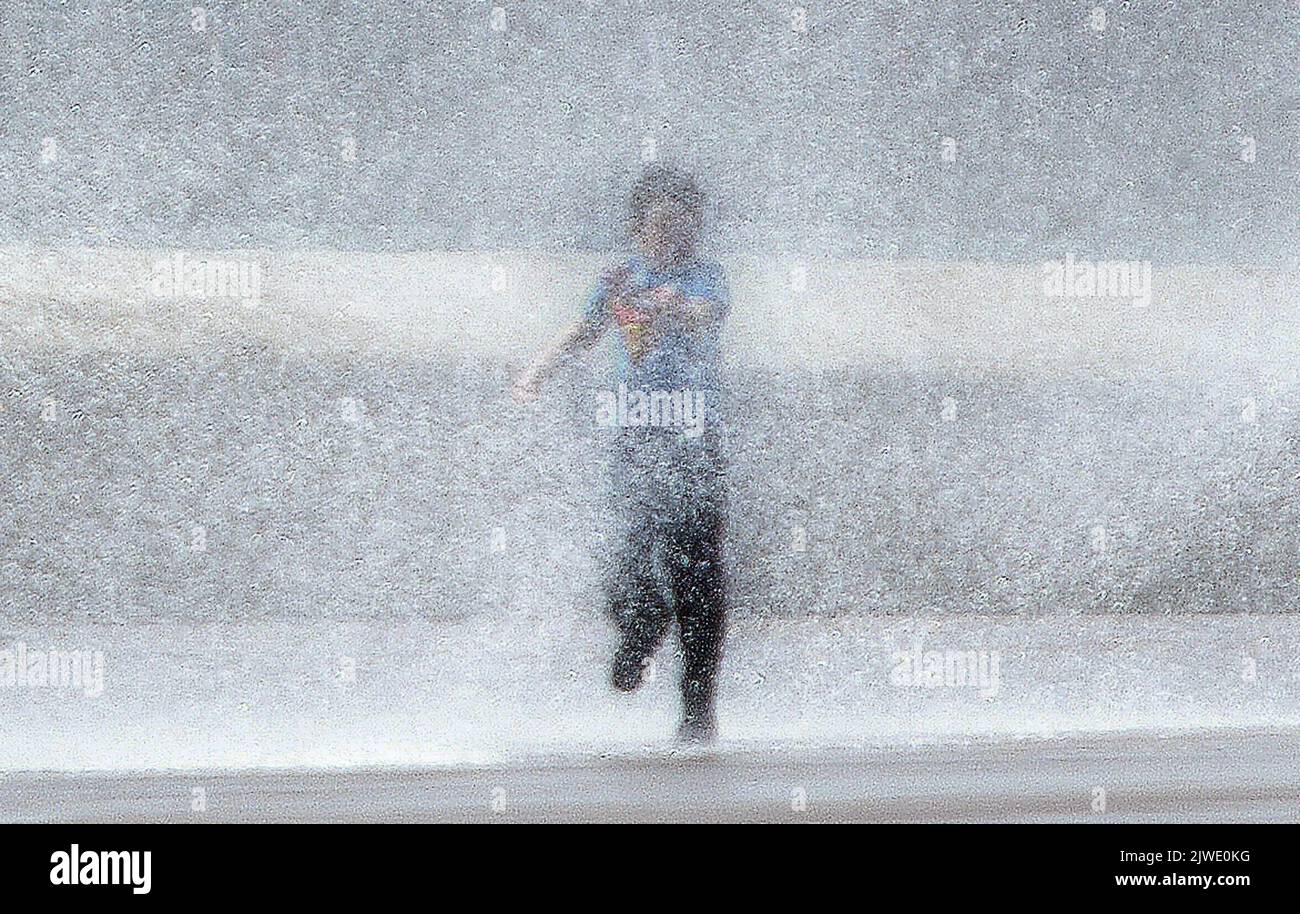 A YOUNGSTER GETS CAUGHT IN THE SPRAY AS WAVES BATTER THE SEAFRONT AT ...