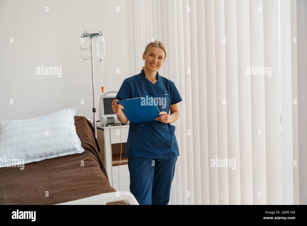 Smiling nurse holding tablet while stands in hospital ward ready to ...