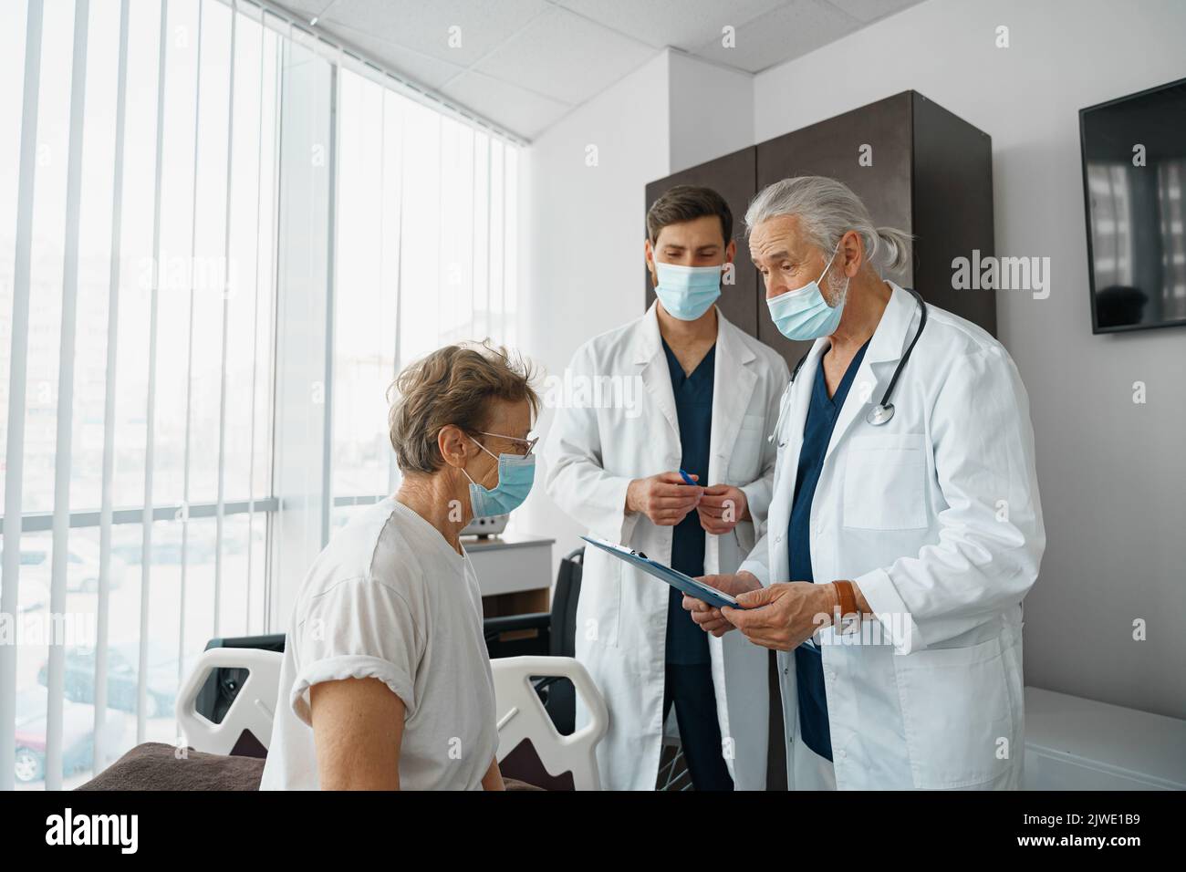 Doctors in masks explain to a sick patient in a wheelchair her ...