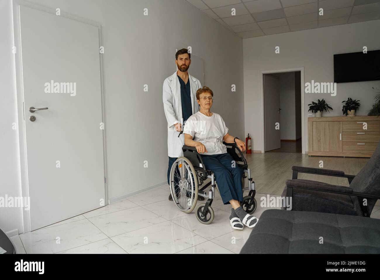 Professional male doctor carrying female patient on wheelchair in ...
