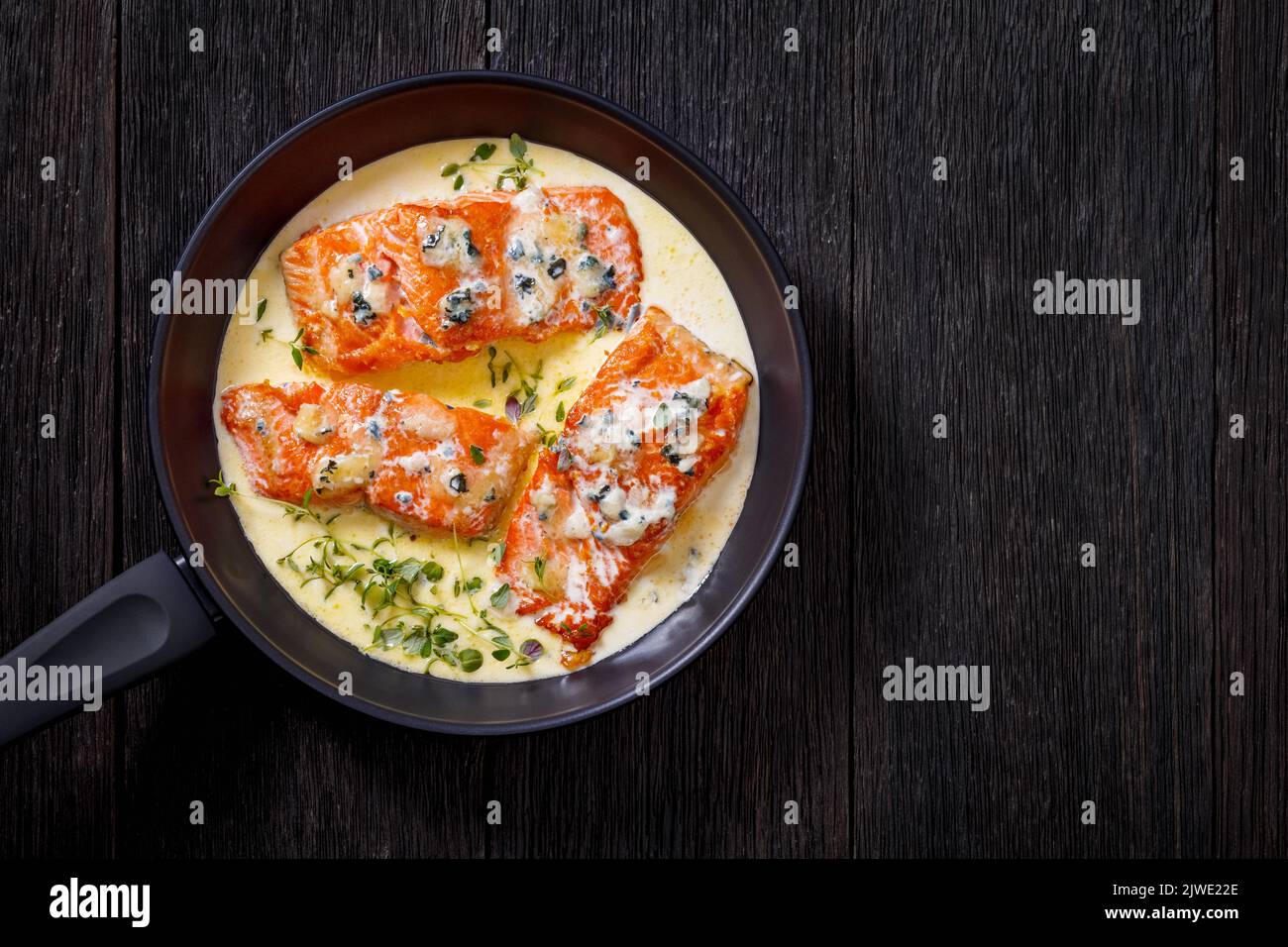 salmon fillet cooked with creamy blue mold cheese sauce in pan on dark ...