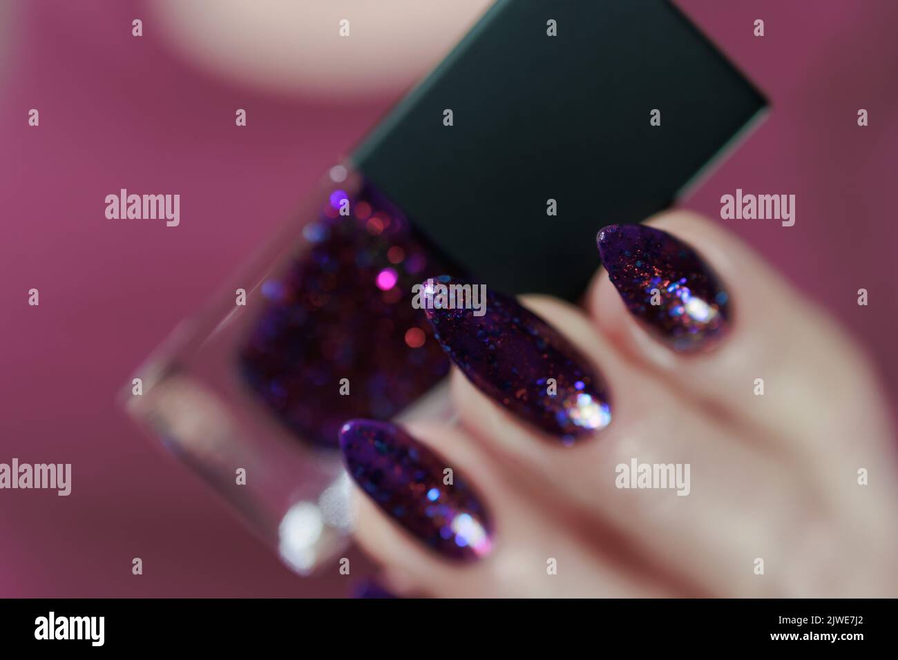 Female hand with long nails and purple plum manicure holds a bottle of ...