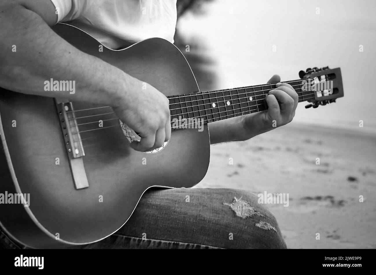 A guy plays an acoustic six-string guitar on a sandy beach near a body ...