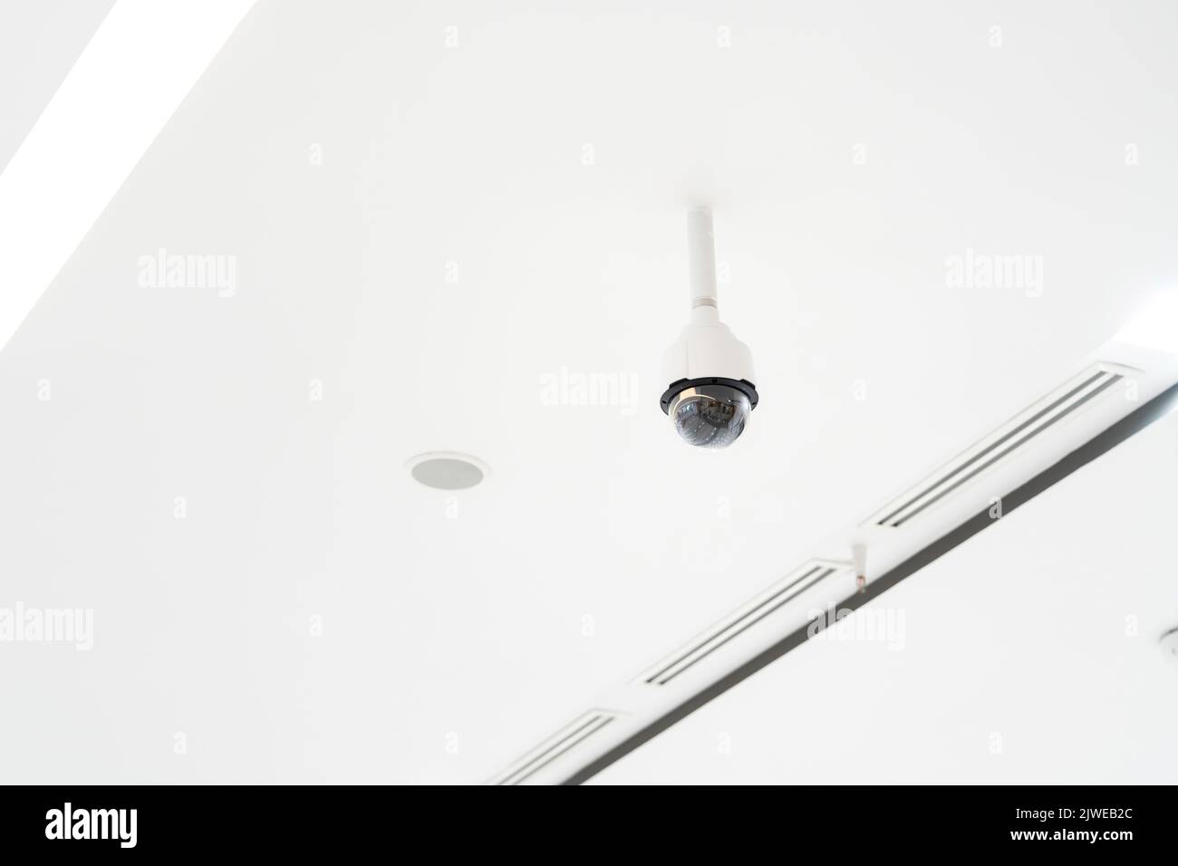 White Closed circuit television CCTV is hung on a white ceiling beside ...