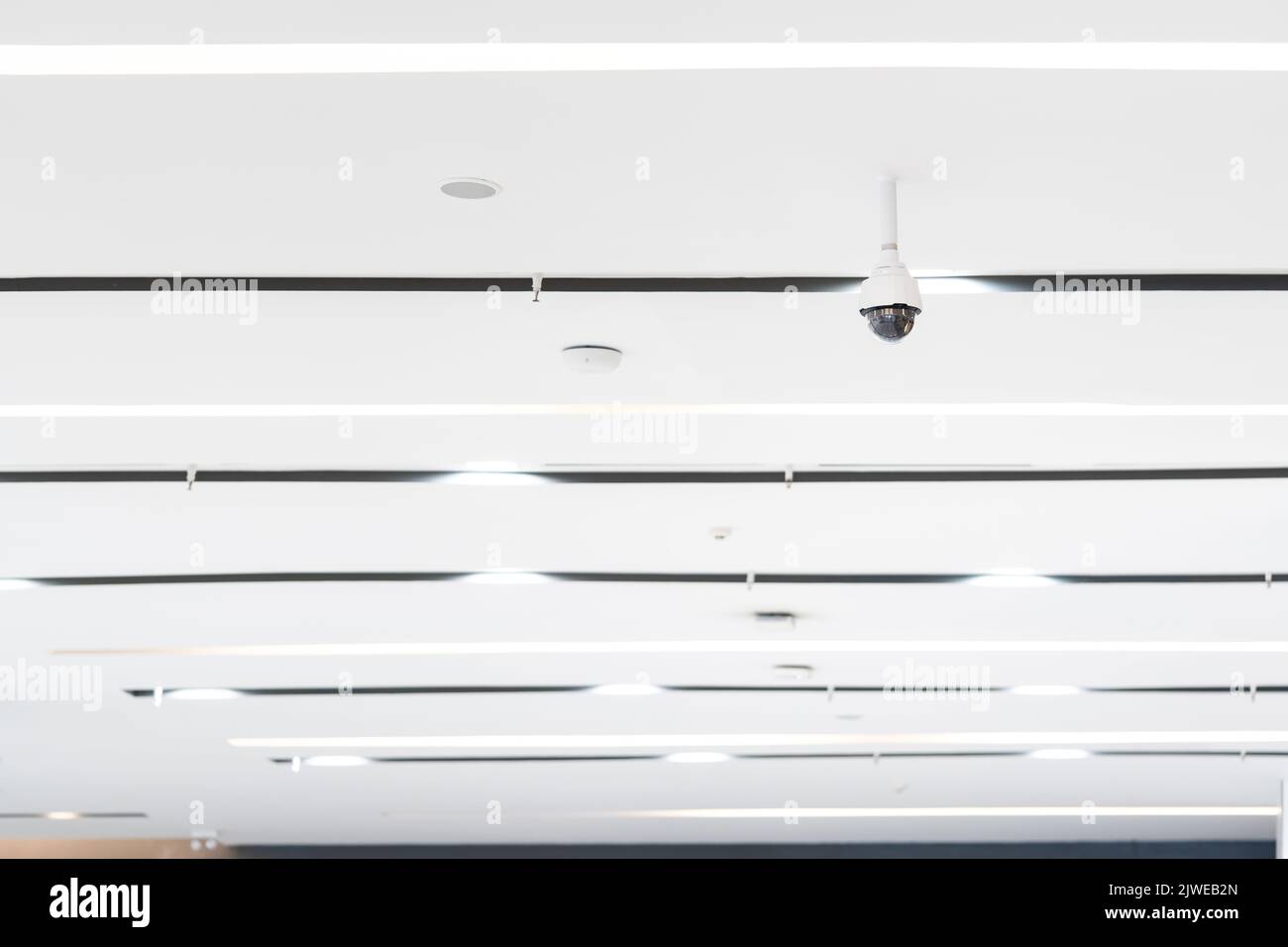 White Closed circuit television CCTV is hung on a white ceiling beside ...