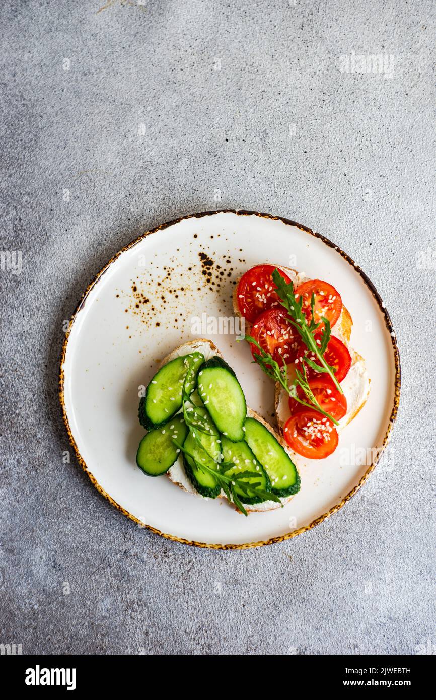 Overhead view of two slices of toast with cream cheese, cucumber ...