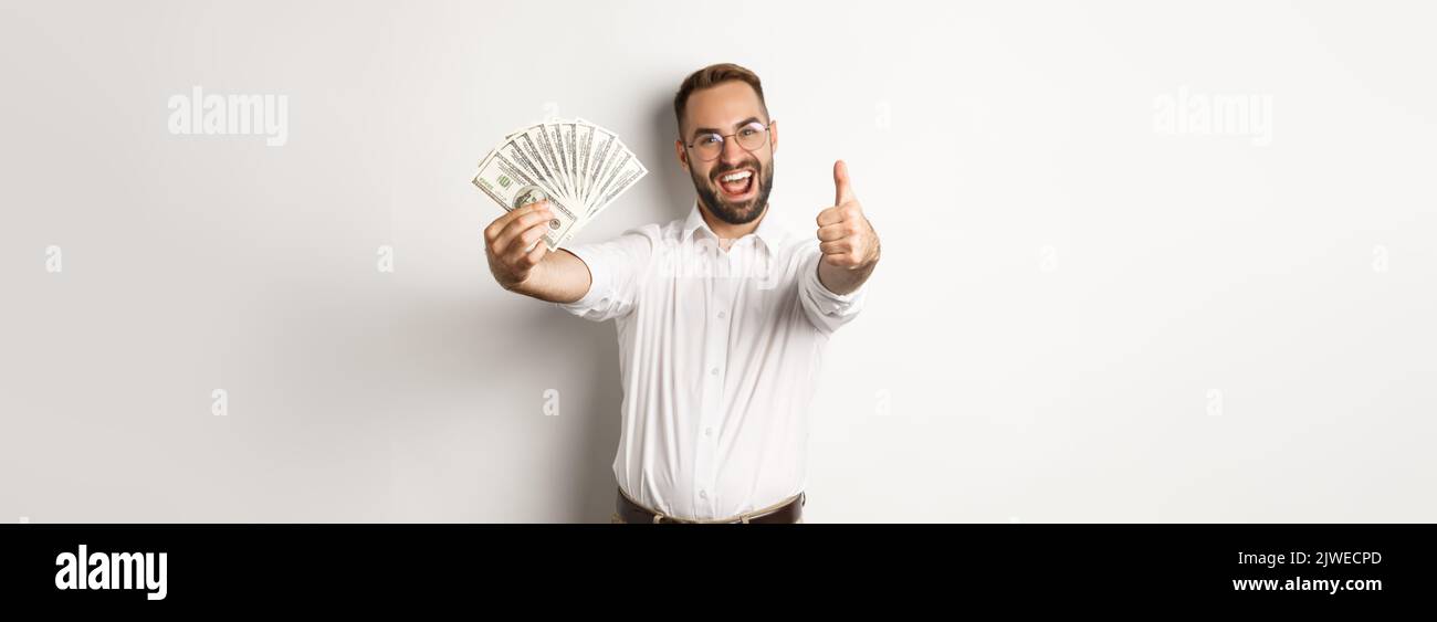 Excited man showing thumbs up and money, earning cash, standing over ...