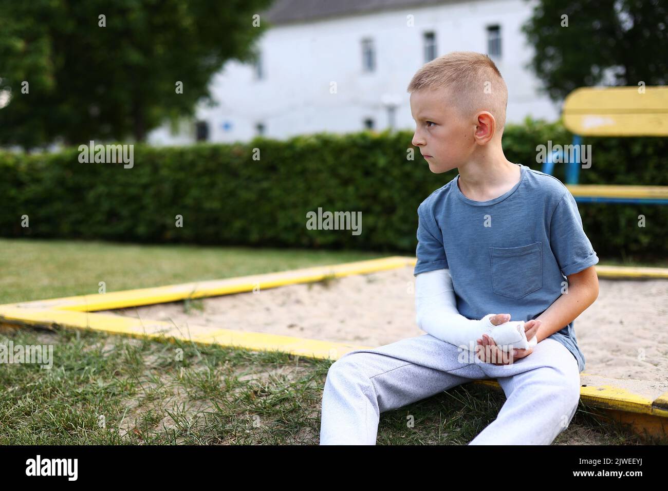 child caucasian with broken limb outdoors sits near the playground and ...