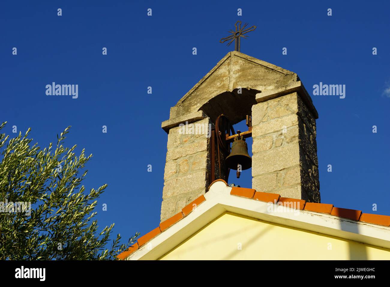 Ancient belfry with a metal cross on a blue sky background by the olive ...