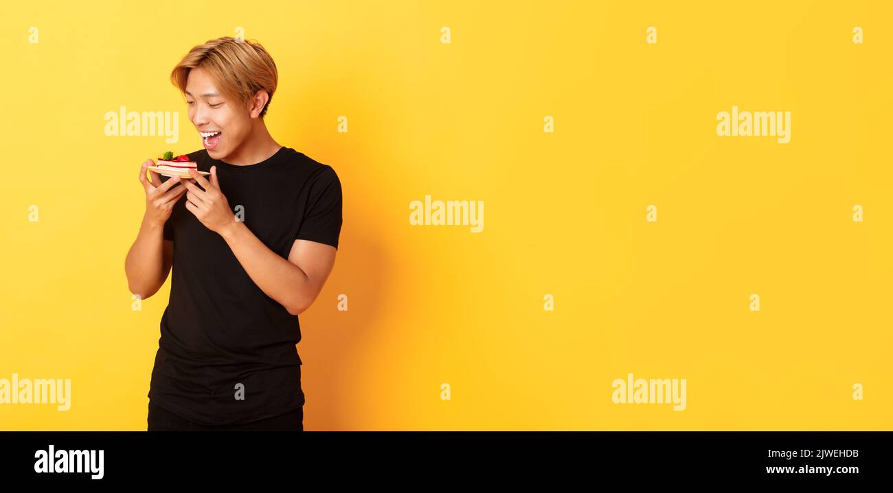 Joyful handsome asian guy smiling and looking tempted at cake while ...