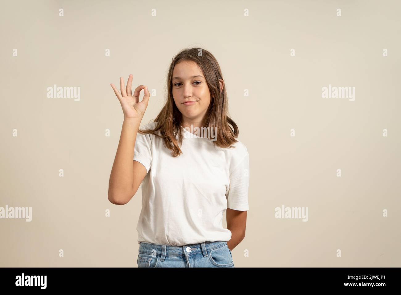 Portrait of cheerful brunette teenager in white t-shirt showing ok sing ...