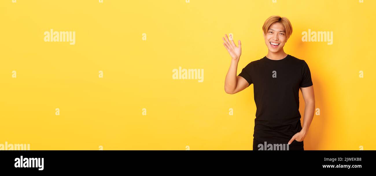 Portrait of handsome friendly asian guy in black outfit, waving hand to ...