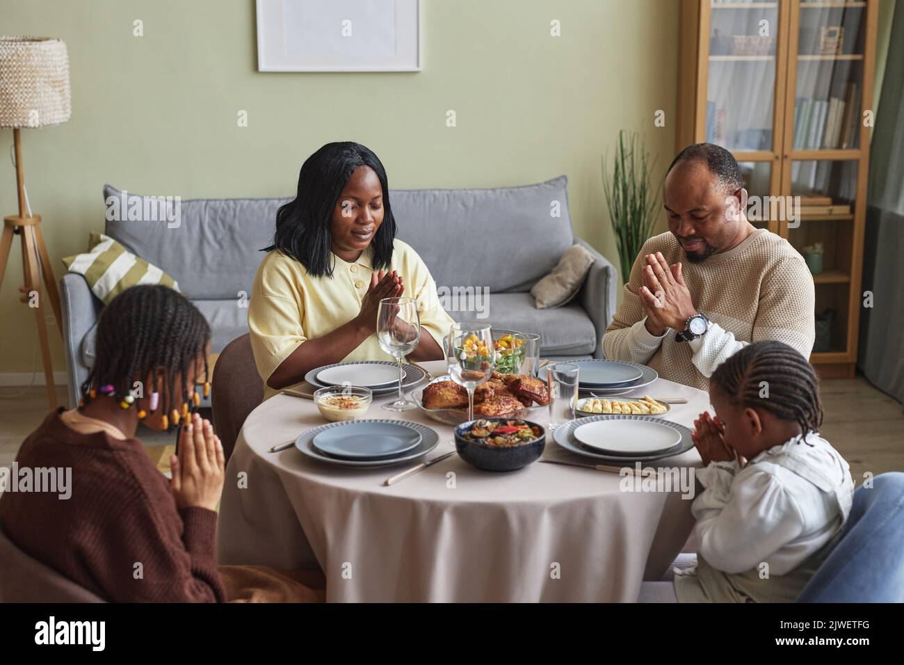 African family of four sitting at dining table and praying before ...