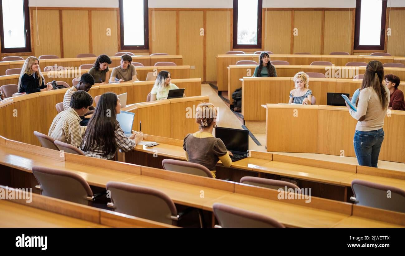 Group of students in a circular classroom with the teacher explaining ...