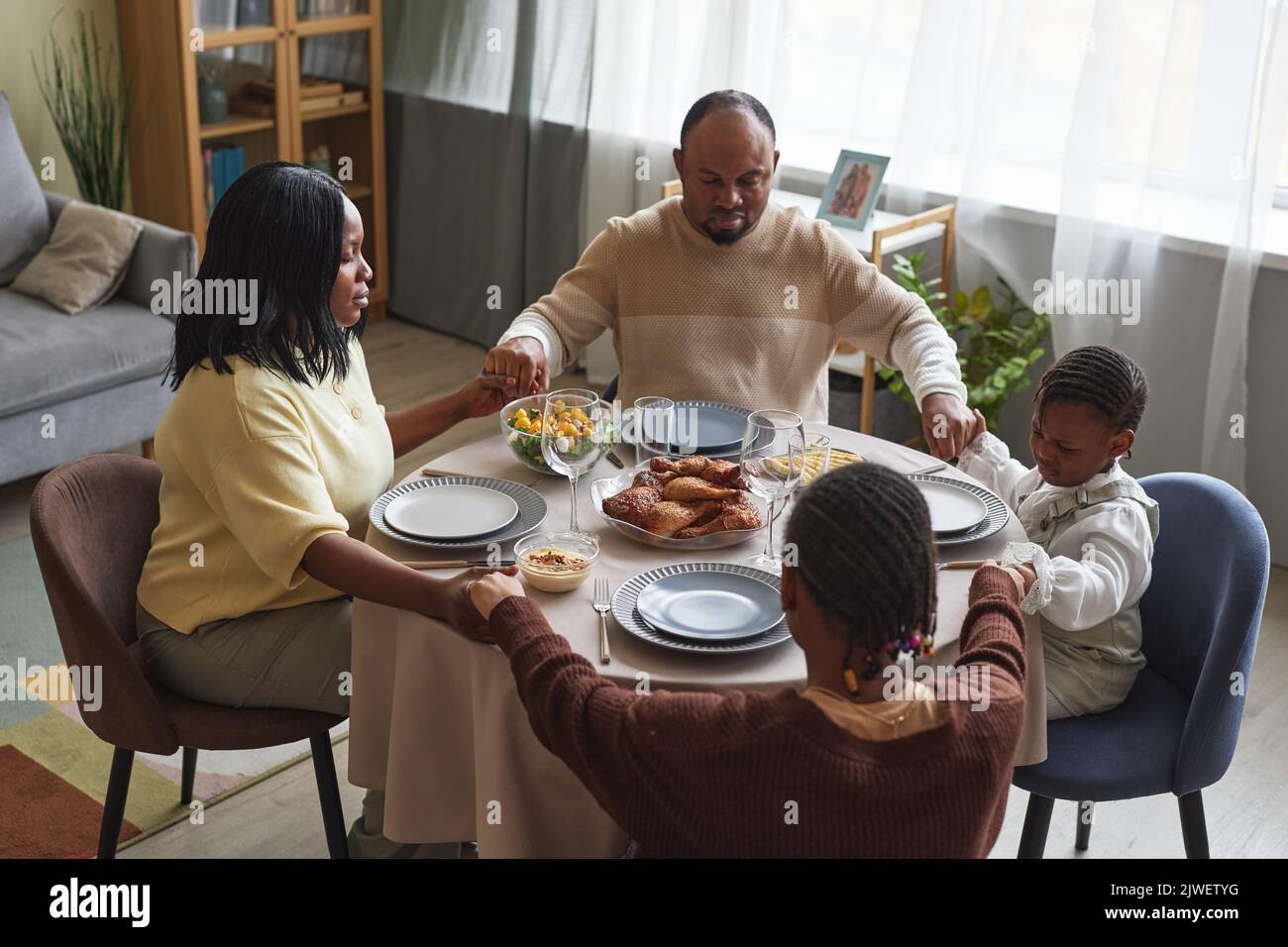 African family with children sitting at dining table with eyes closed ...