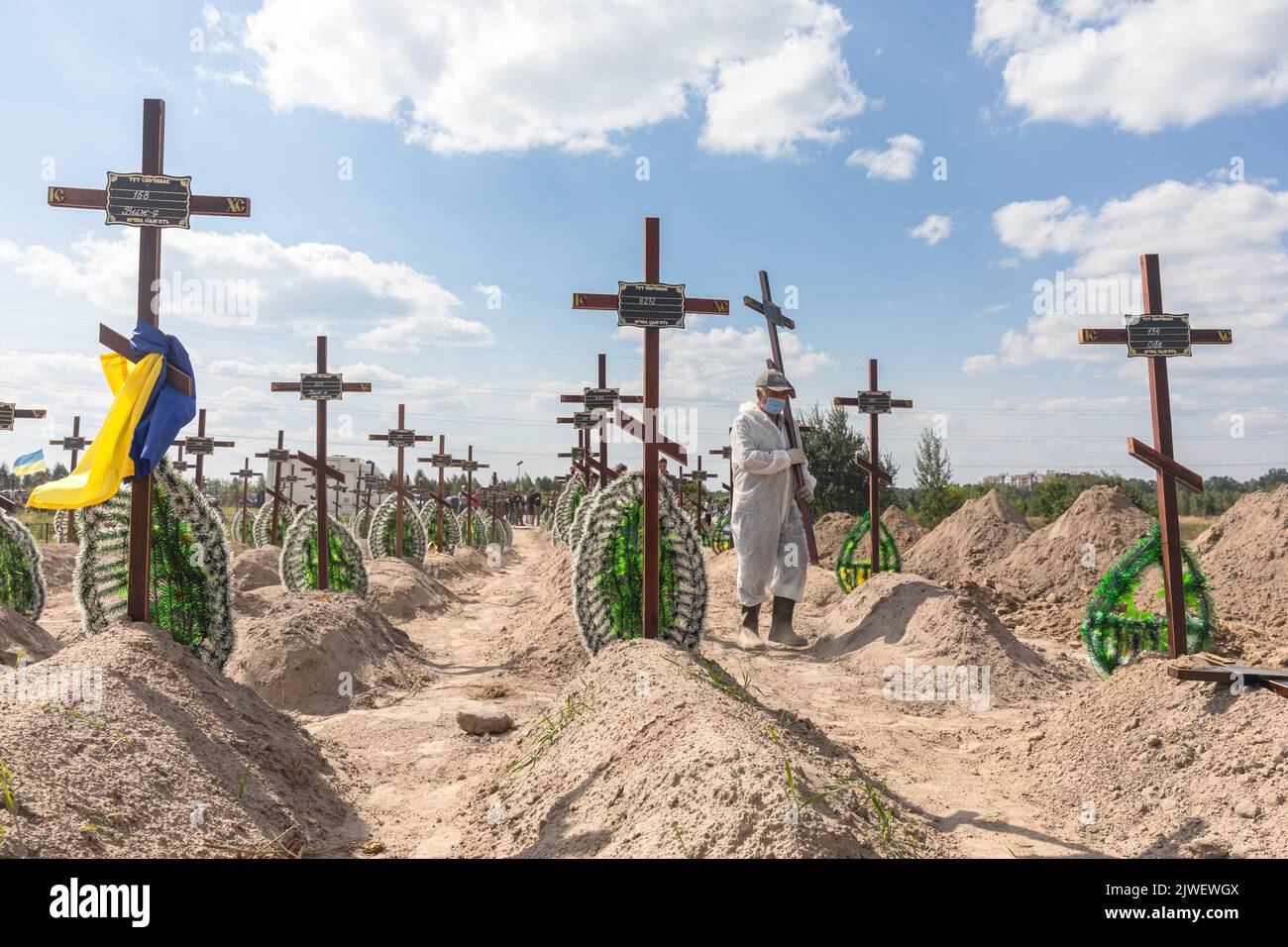 A Man In A Protective Suit Carries A Funeral Cross To A Fresh Grave
