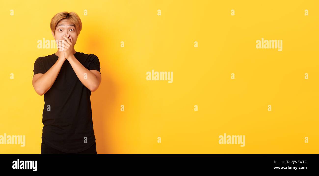 Portrait of surprised gasping asian guy with blond haircut, cover mouth ...