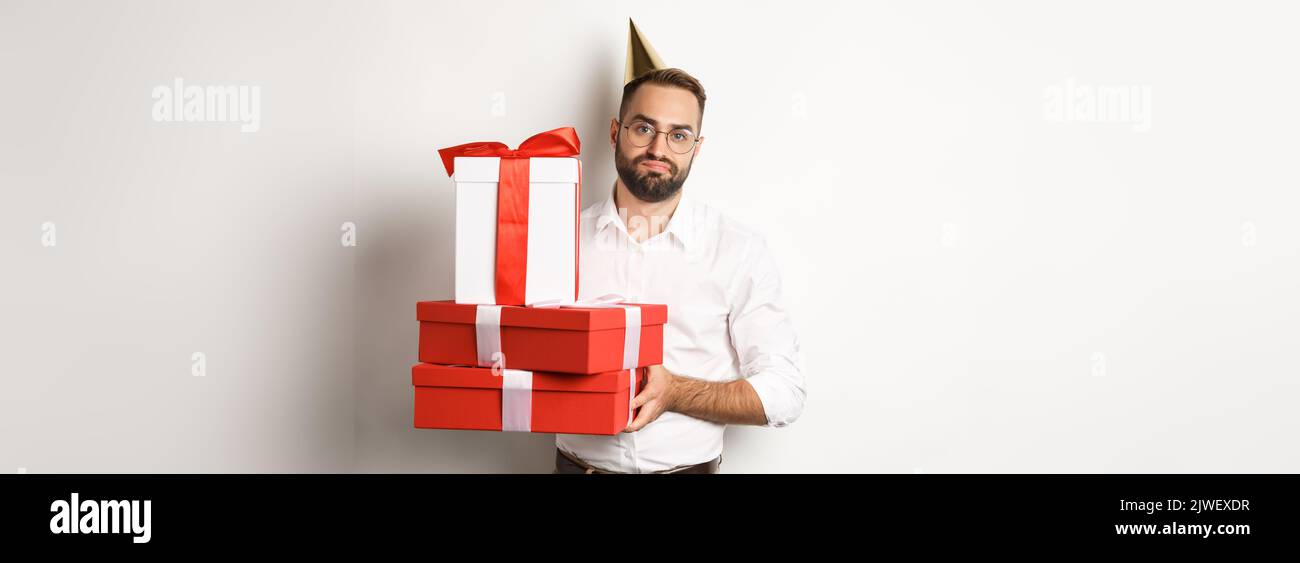 Holidays and celebration. Displeased guy holding birthday gifts and ...