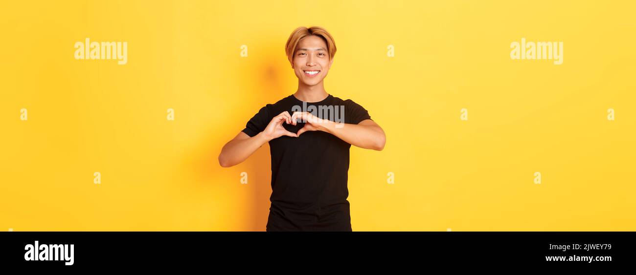 Portrait of lovely handsome blond asian man, showing heart gesture and ...