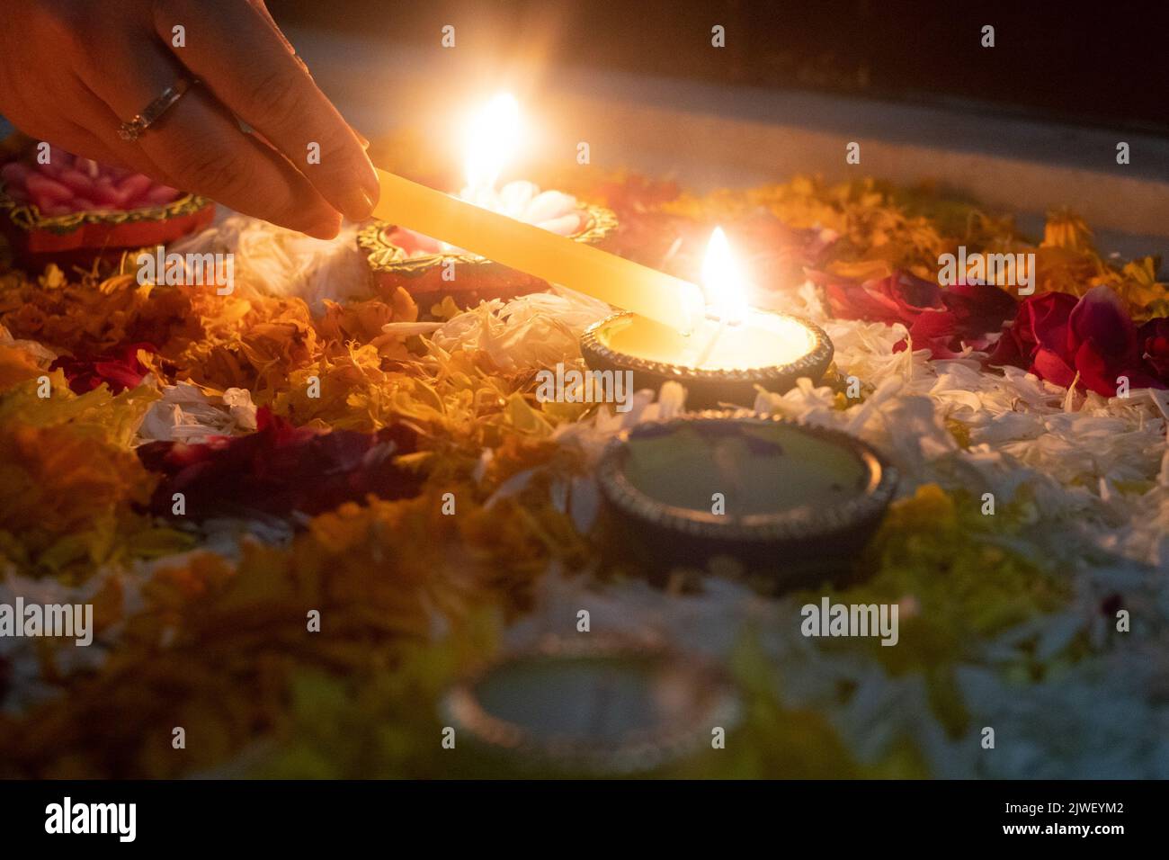 soft filter shot of person lighting diya oil lamp with a lit candle set ...