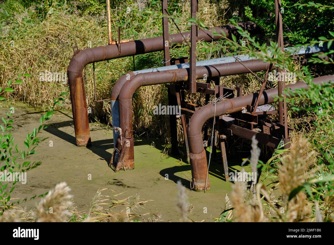 Old rusty water pump pipes go into dirty pond polluted with industrial ...
