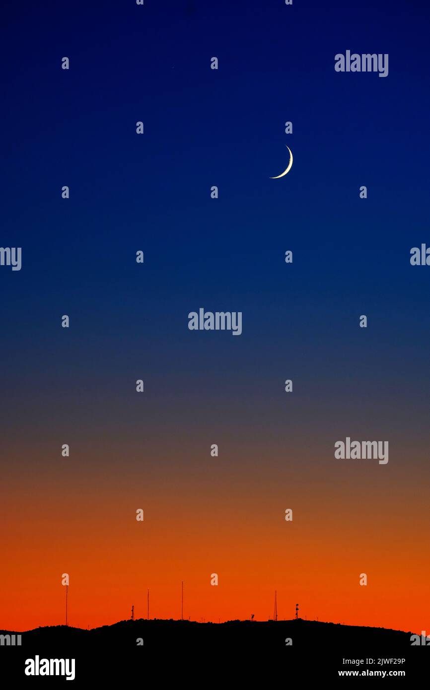 Cresent moon on the horizon at twilight setting with orange glow sunset ...
