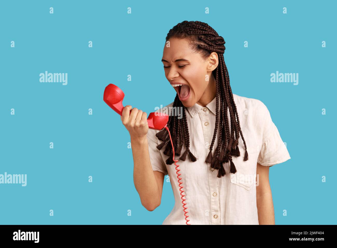 Portrait of woman with black dreadlocks screaming into phone handset ...