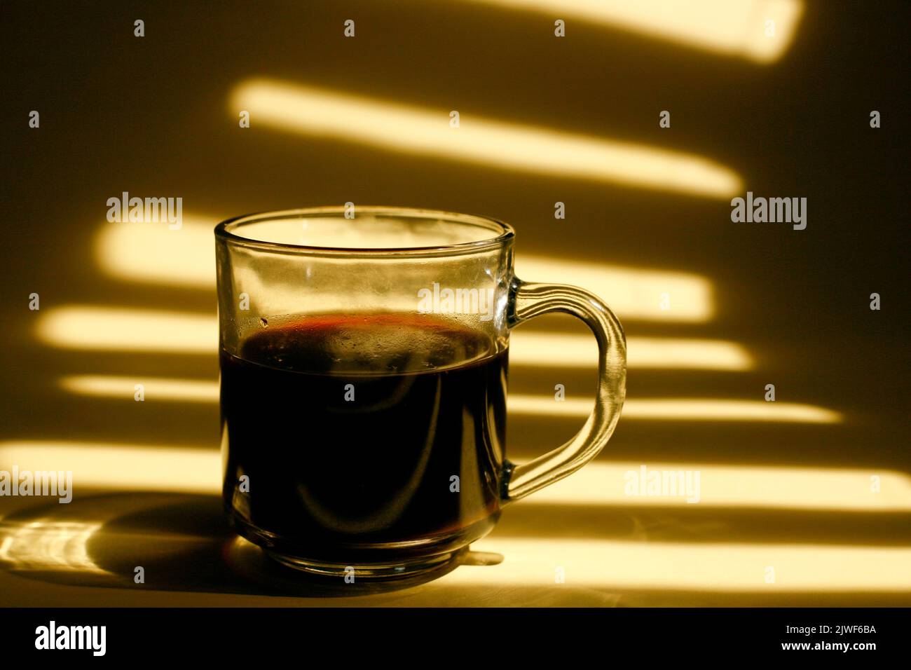 close up of glass cup of coffee with light and shadow in the background ...