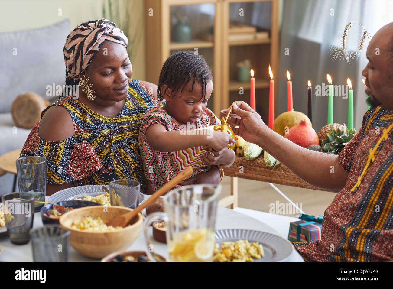 African little girl opening present together with her parents giving ...