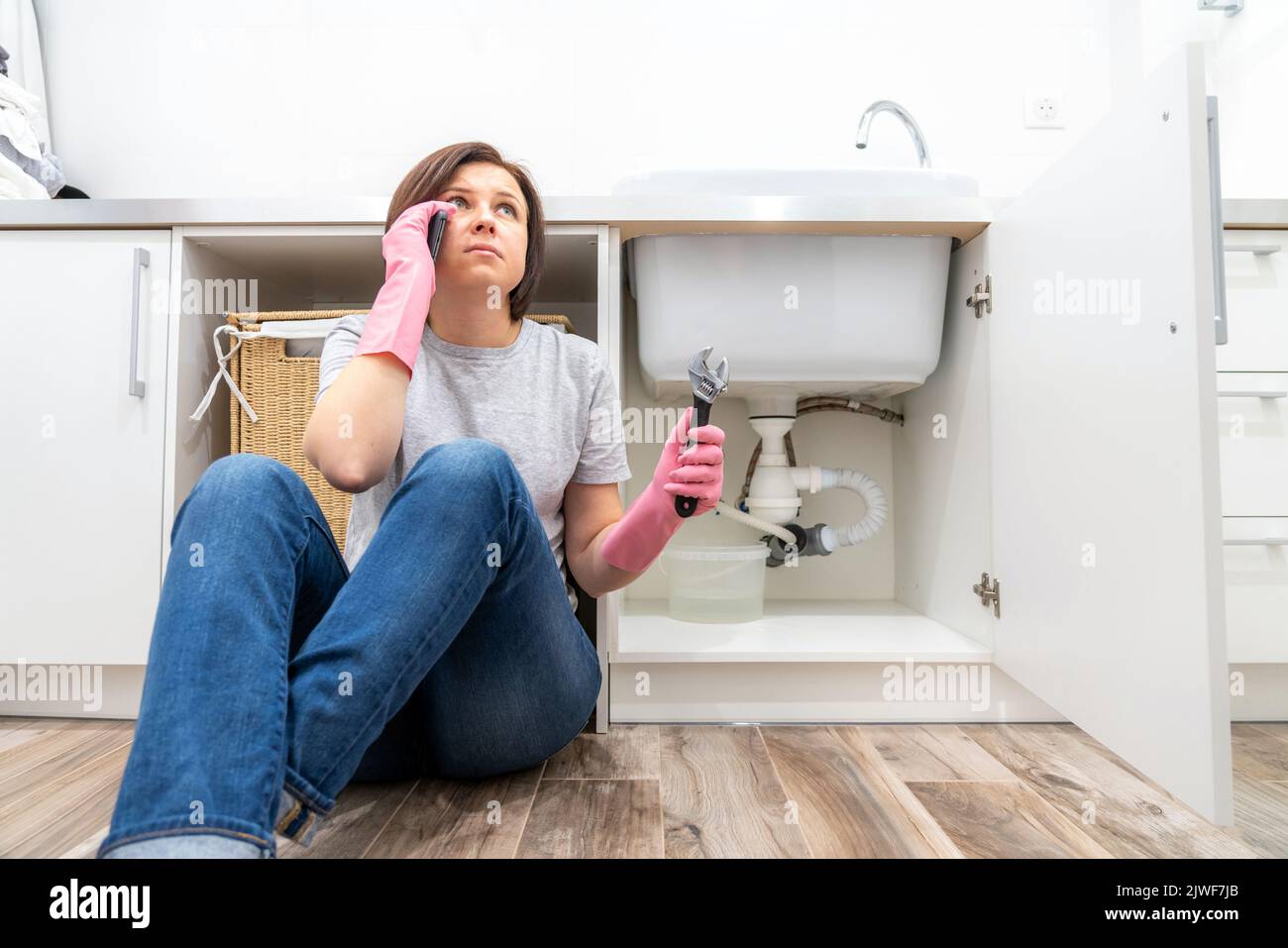 Woman sitting near leaking sink in laundry room calling for help Stock ...
