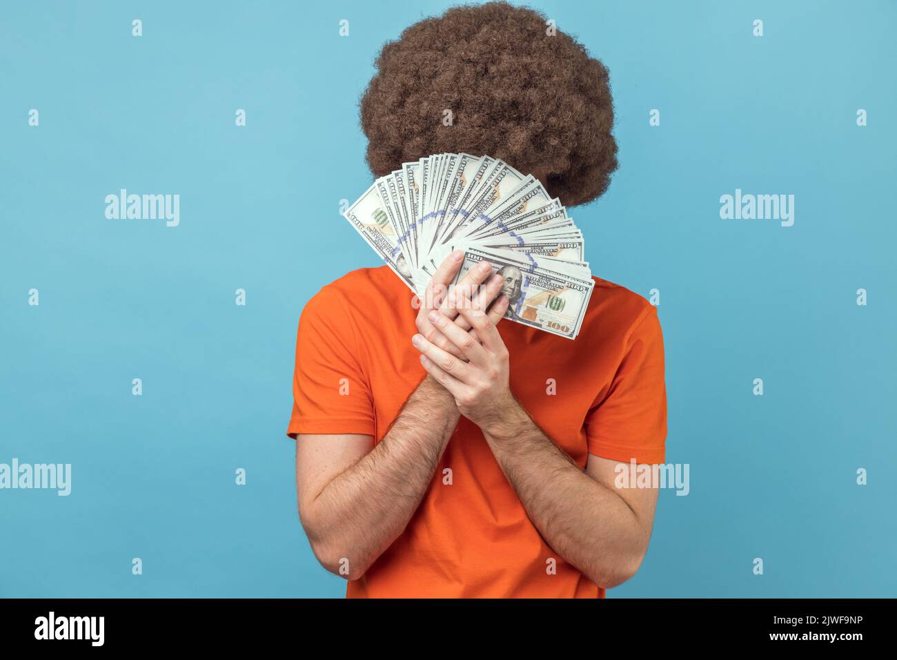 Portrait of man with Afro hairstyle wearing orange T-shirt hiding face ...