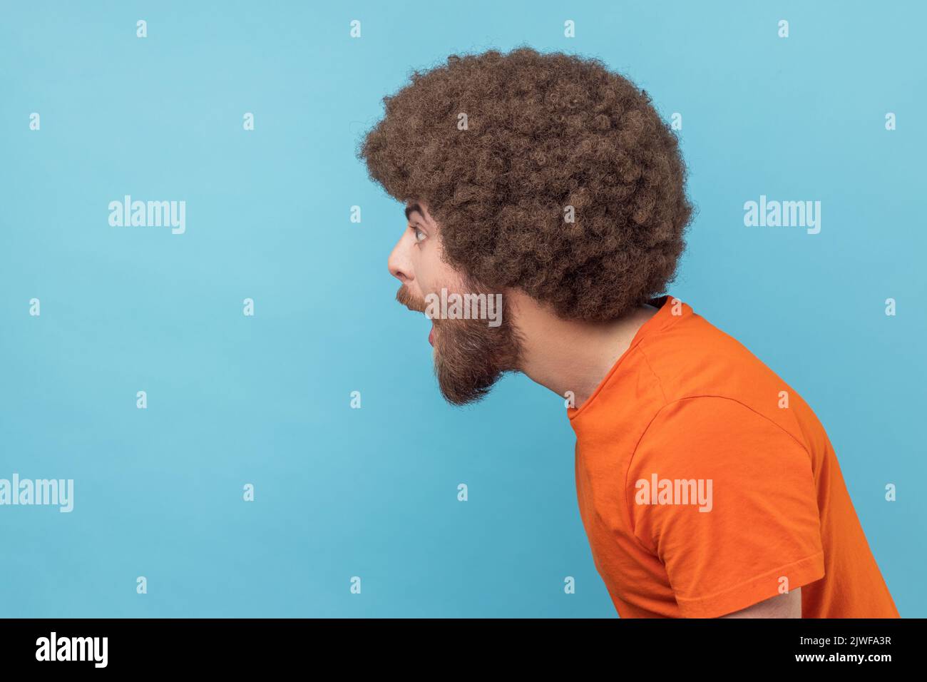 Side view of amazed man with Afro hairstyle wearing orange T-shirt ...