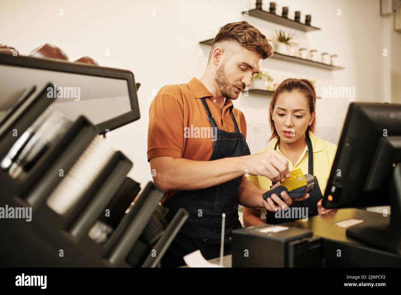 Coffeeshop worker explaining new worker how to use credit card reader ...