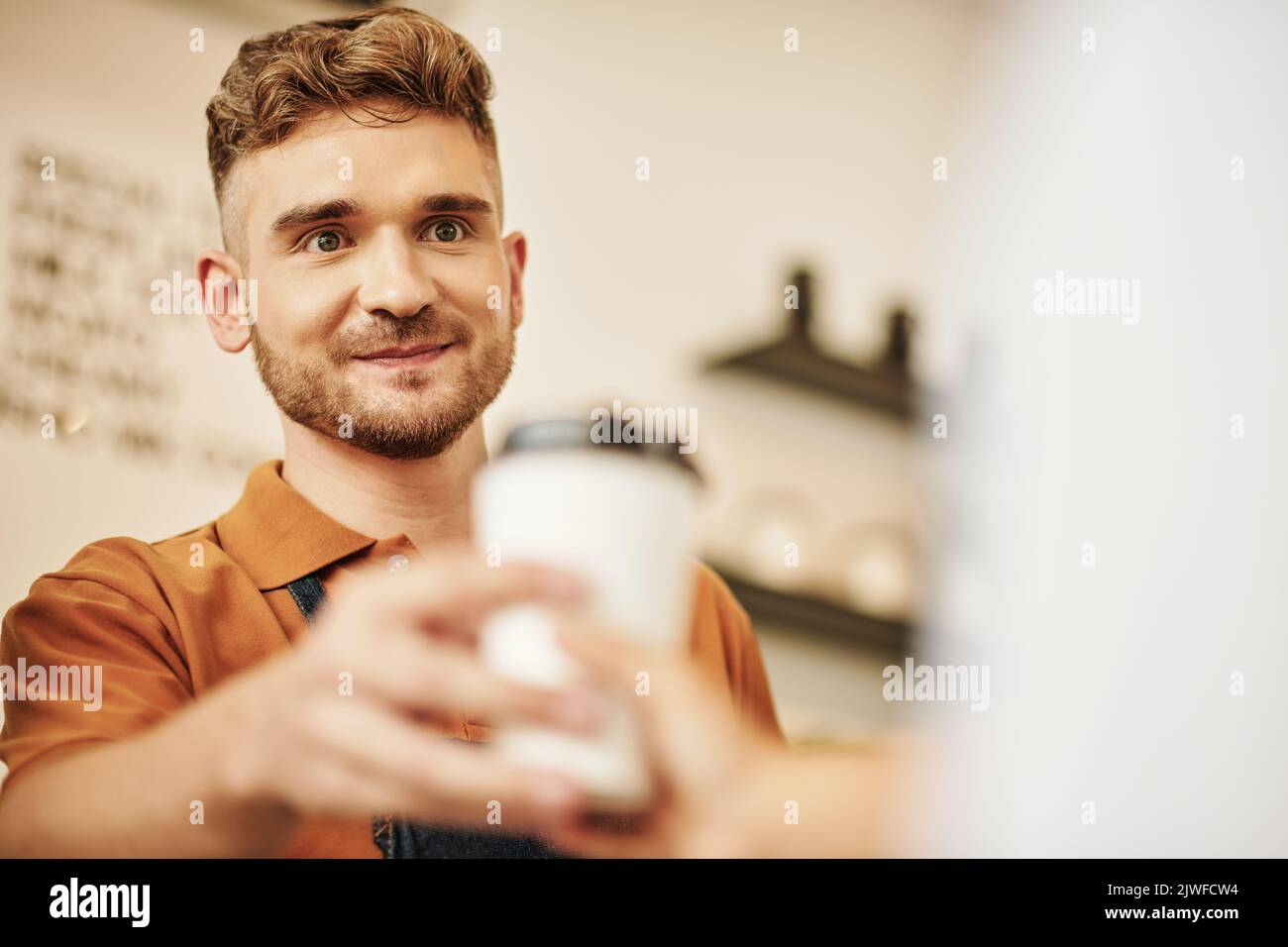 Portrait of smiling coffeeshop barista giving cup of coffee to customer ...