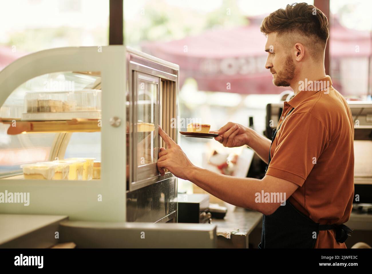Coffeeshop barista taking plate with cake from cafe showcase Stock ...