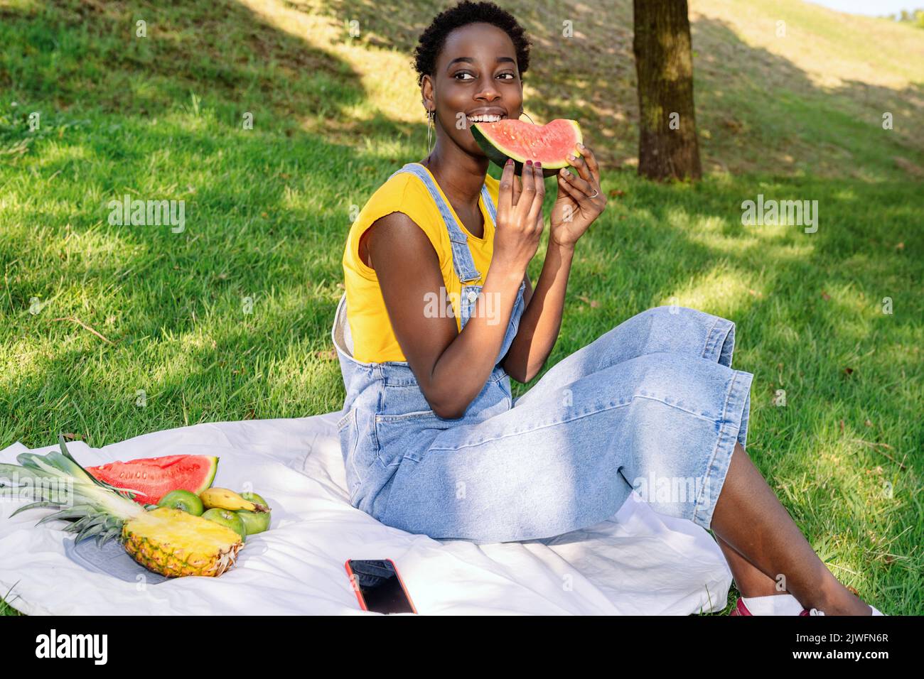 Very happy smiling black African woman sitting in an outdoor park while ...