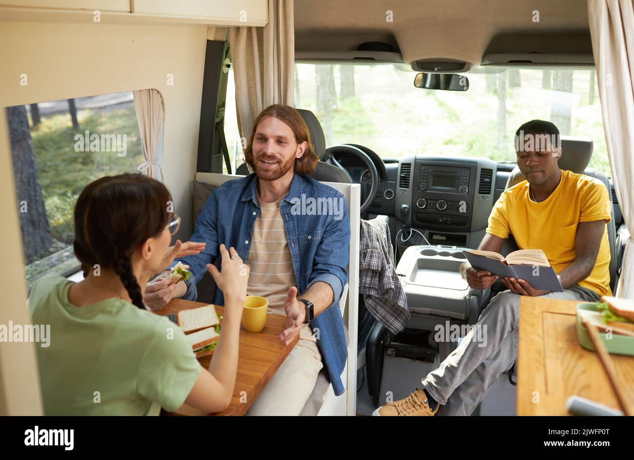 Group of young people having lunch and reading a book while resting in ...