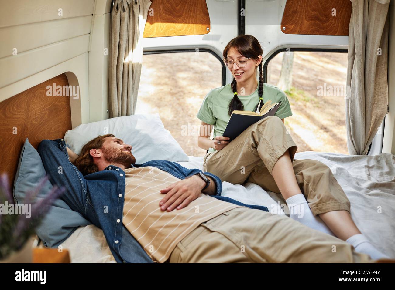 Young couple relaxing on bed together and reading a book in motorhome ...