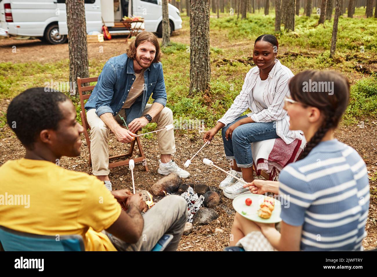 Group of young friends frying marshmallow on fire outdoors during ...