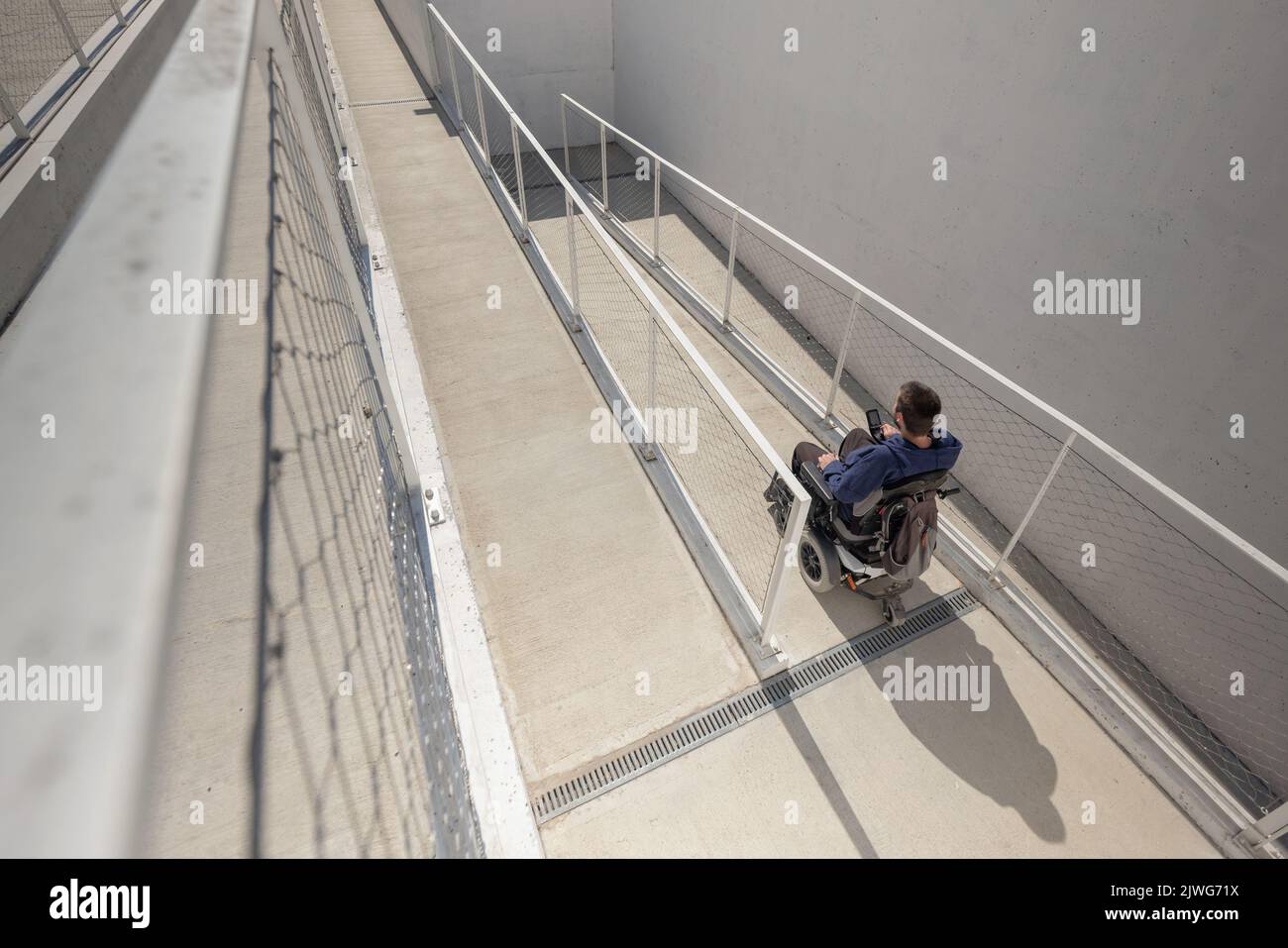 Man on electric wheelchair moving along concrete accessibility pathway ...