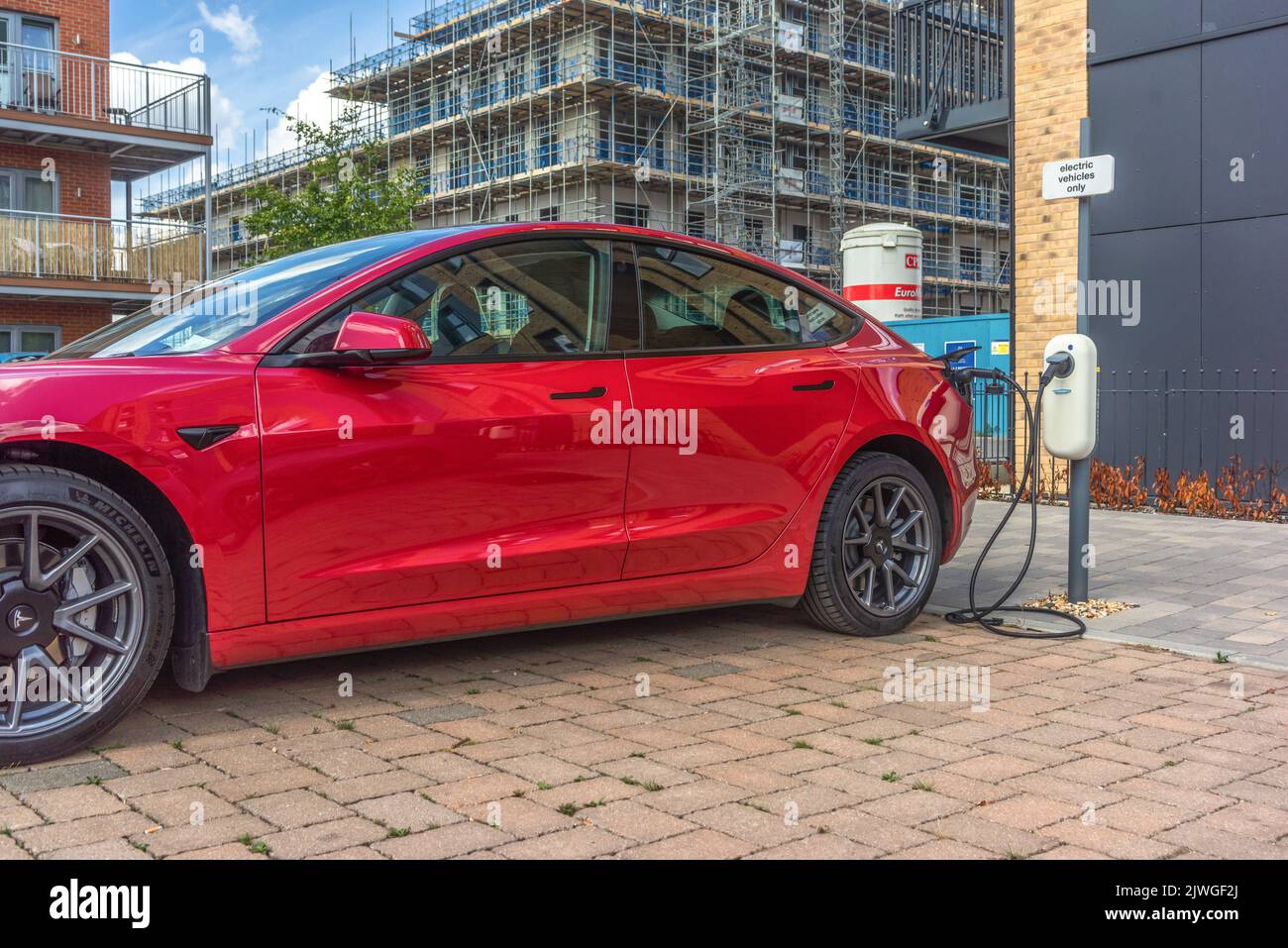 A red Tesla car is charging its car battery at an electrical vehicle ...