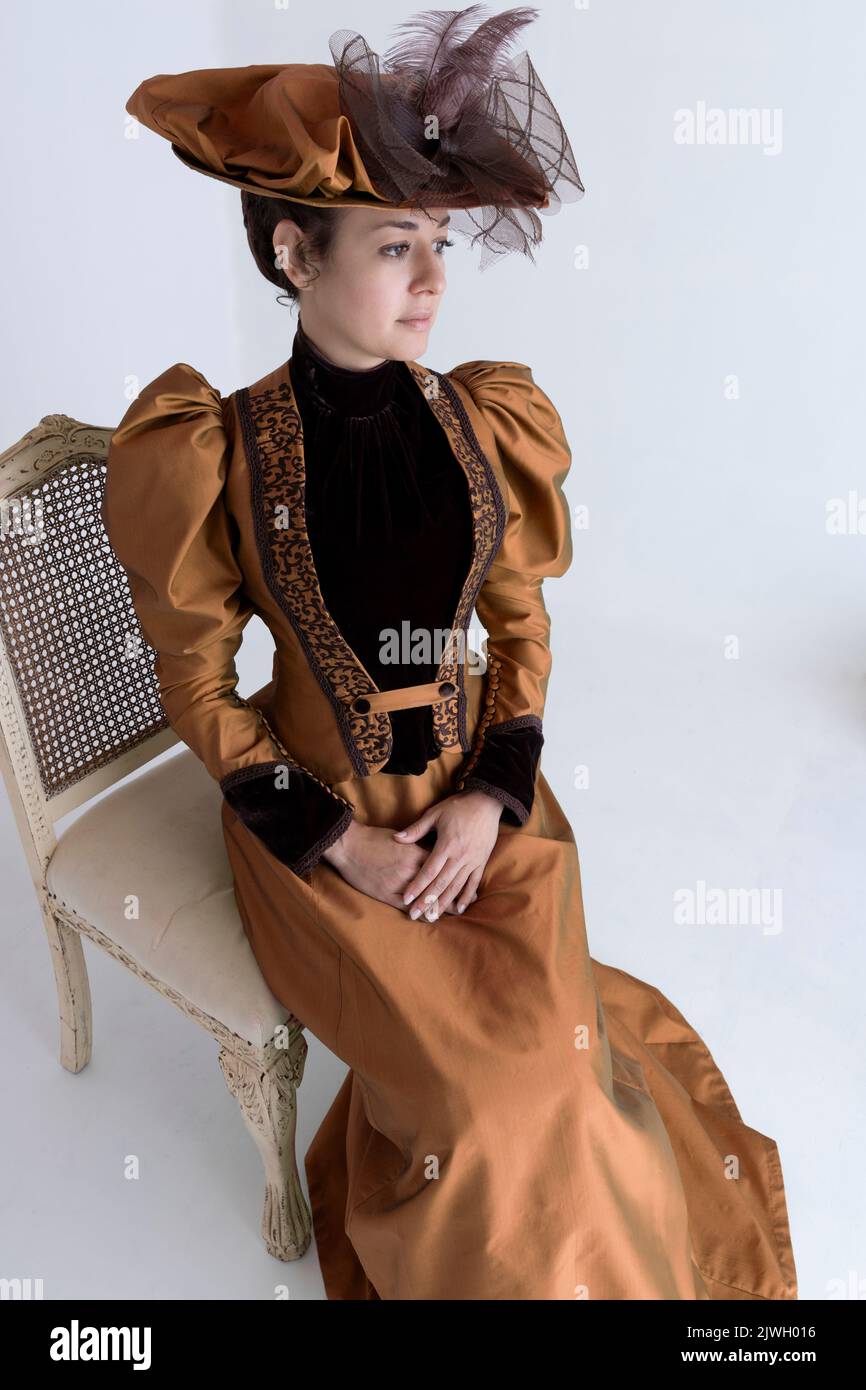 A Victorian woman wearing a bronze silk ensemble against a white ...