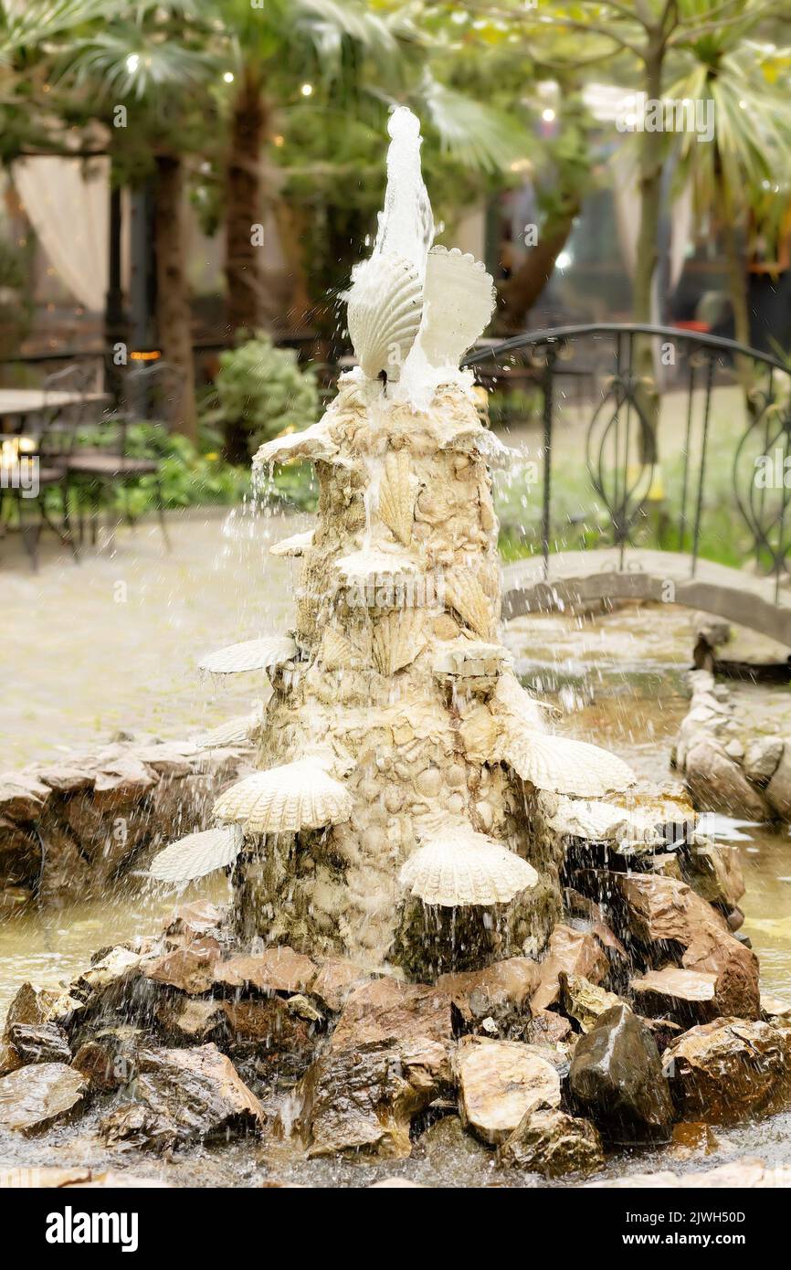 Outdoor decorative fountain with sea shells on the background of a cafe ...