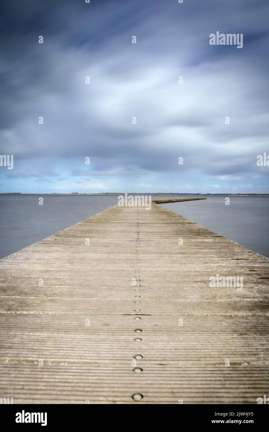 A vertical shot of a jetty in the middle of a lake under a gloomy ...