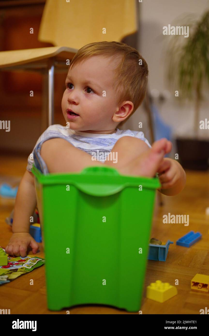 Cute little boy sitting in the plastic box and playing with blocks set ...