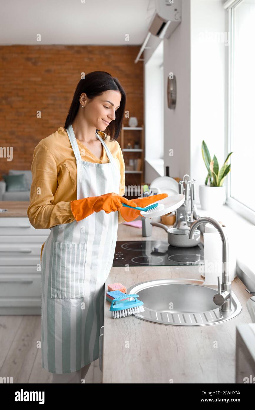Young woman cleaning plate with brush in kitchen Stock Photo - Alamy