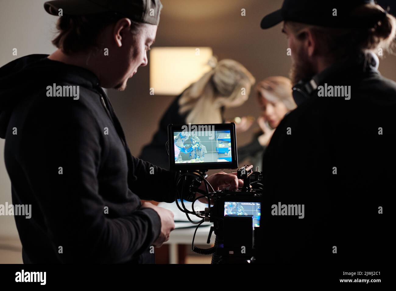 Two young men in black shirts adjusting focus of camera during shooting ...