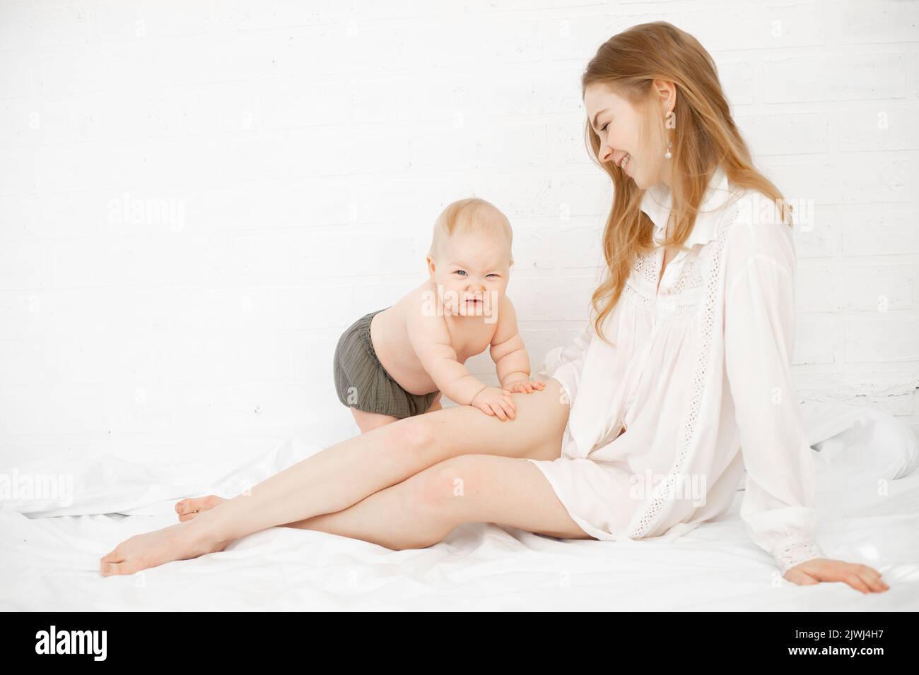 Portrait of young smiling mother with long dark hair in white shirt with little cute plump baby ...