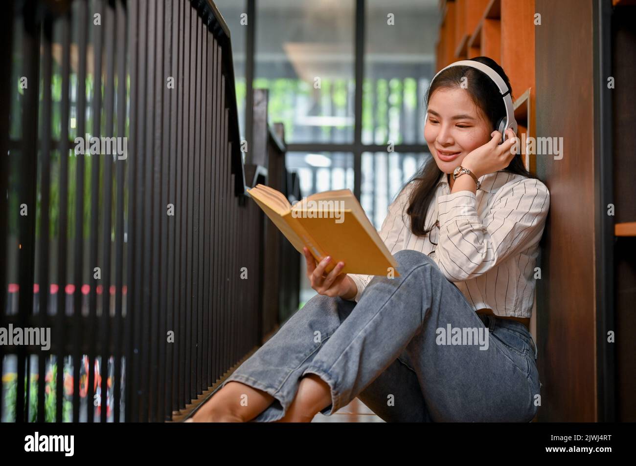 Relaxed and chill young Asian female reading a book in the library ...