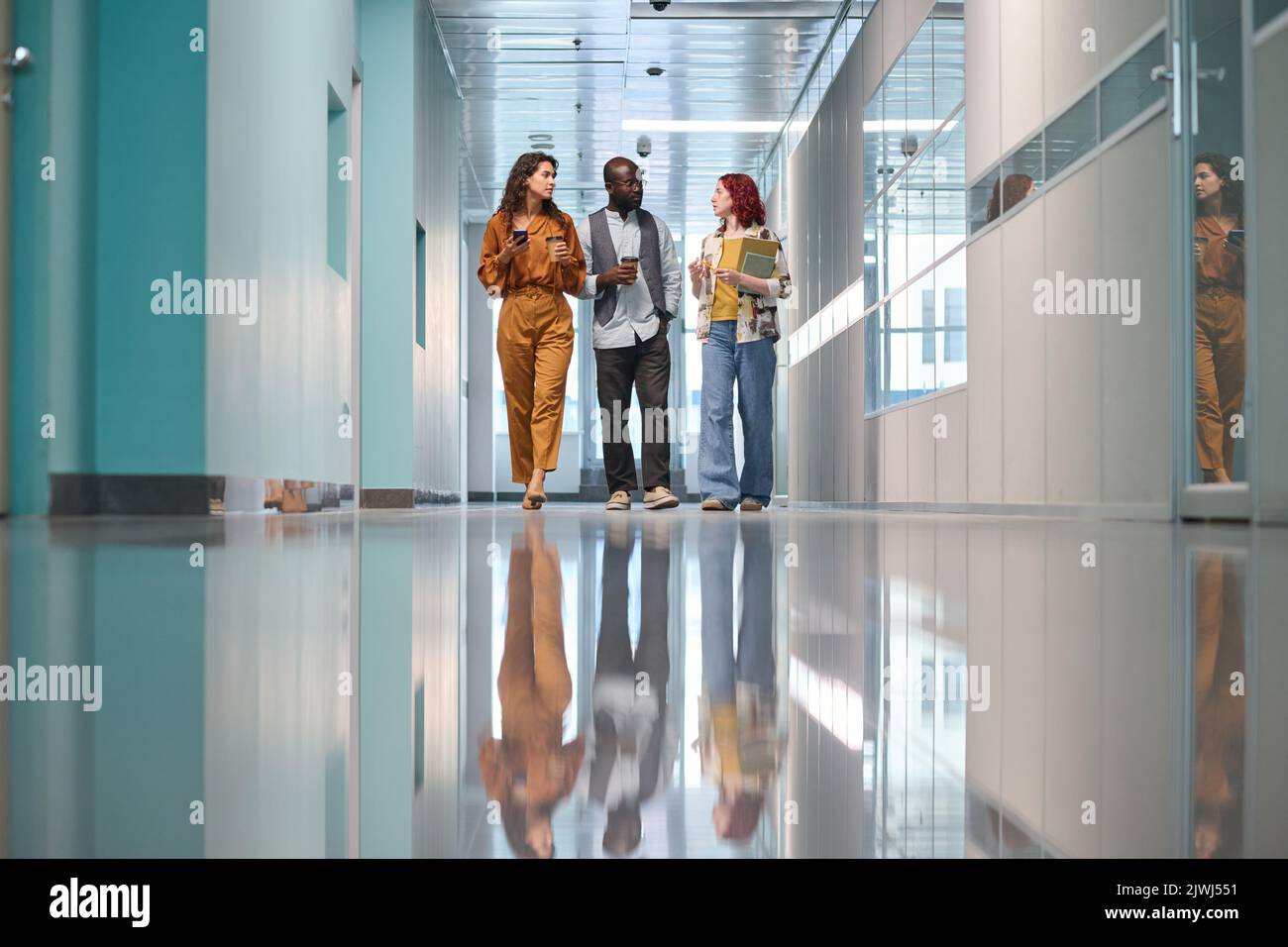 Part of interior of office center and three colleagues walking along ...